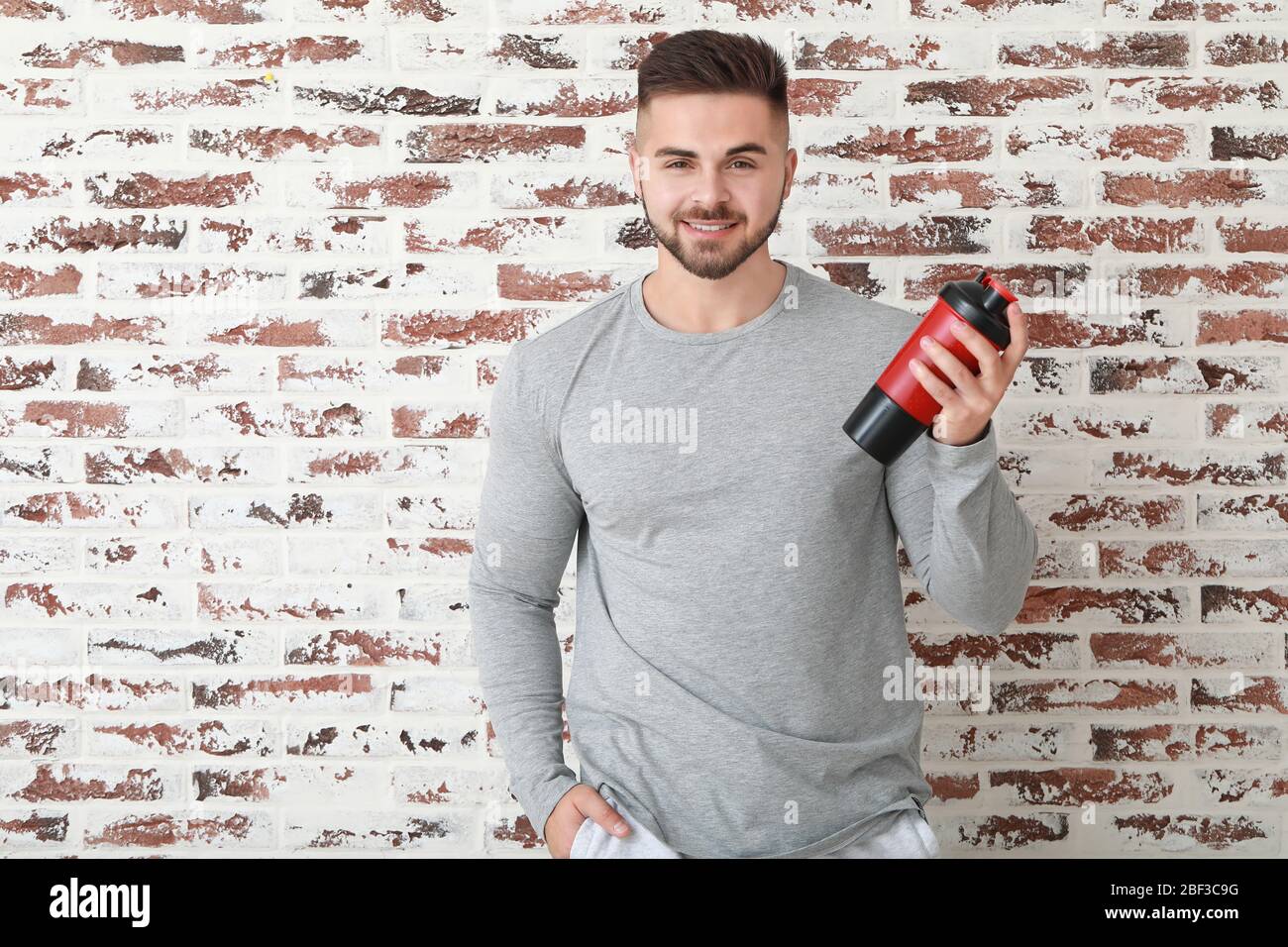 Sporty man with protein shake on brick background Stock Photo - Alamy