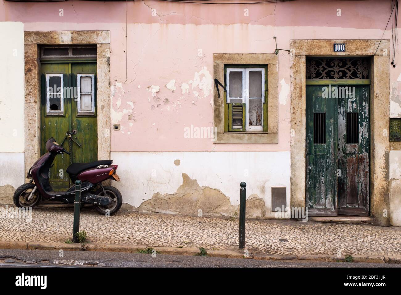 Maroon scooter parked in front of rustic pink building with two green ...