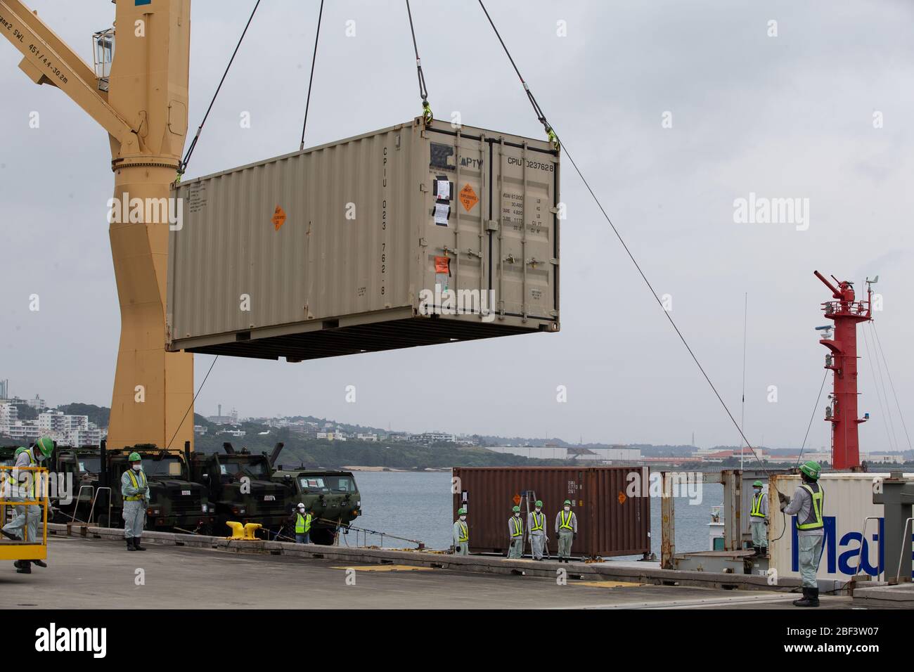 Civilian contractors stabilize a shipping container during a munitions ...
