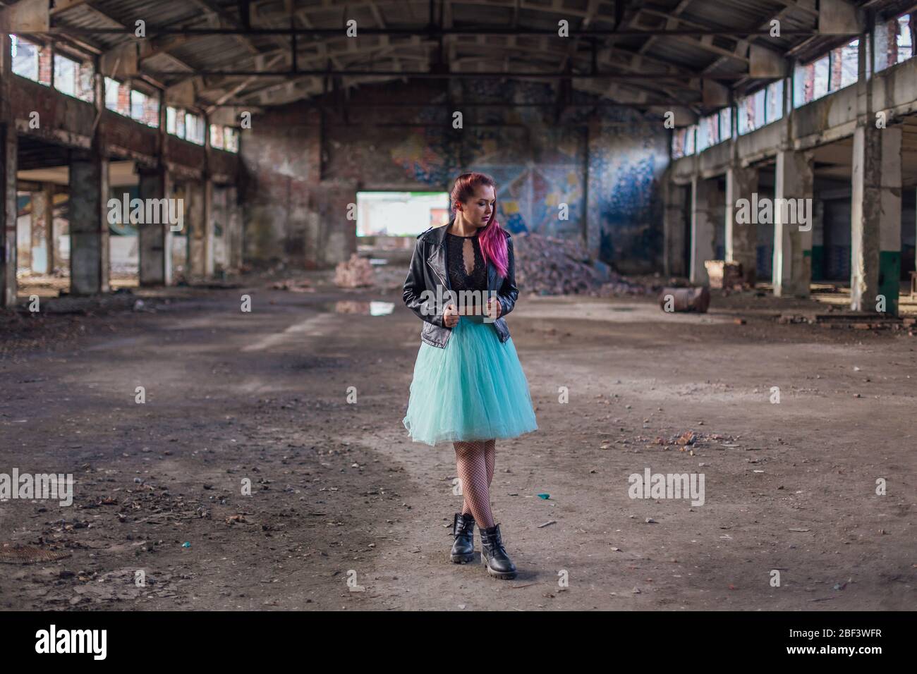 Portrait of a young girl with pink hair standing inside of collapsed ...