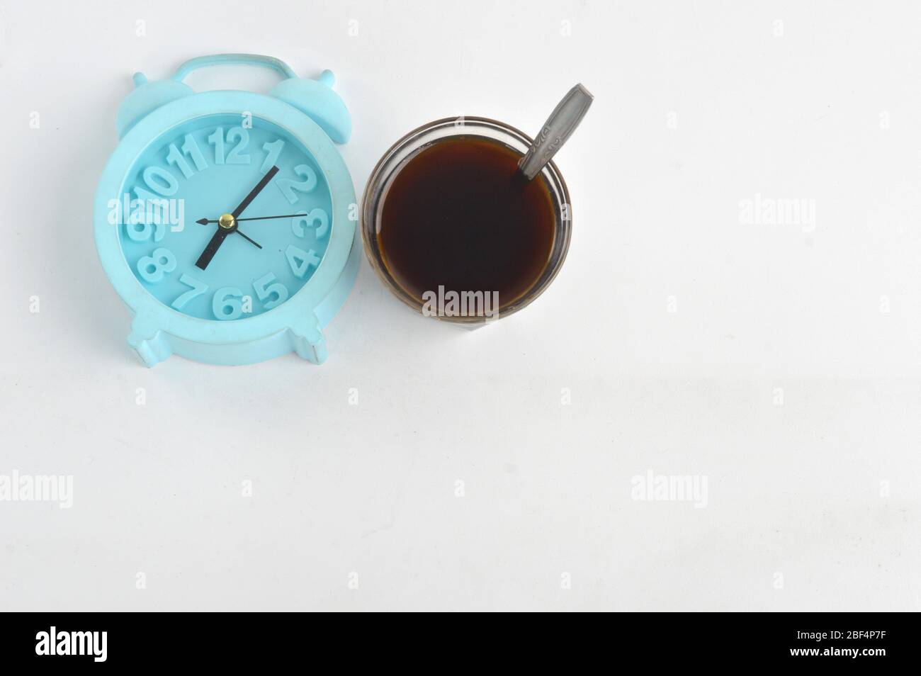 A glass of black coffee and a blue alarm clock isolated on white ...