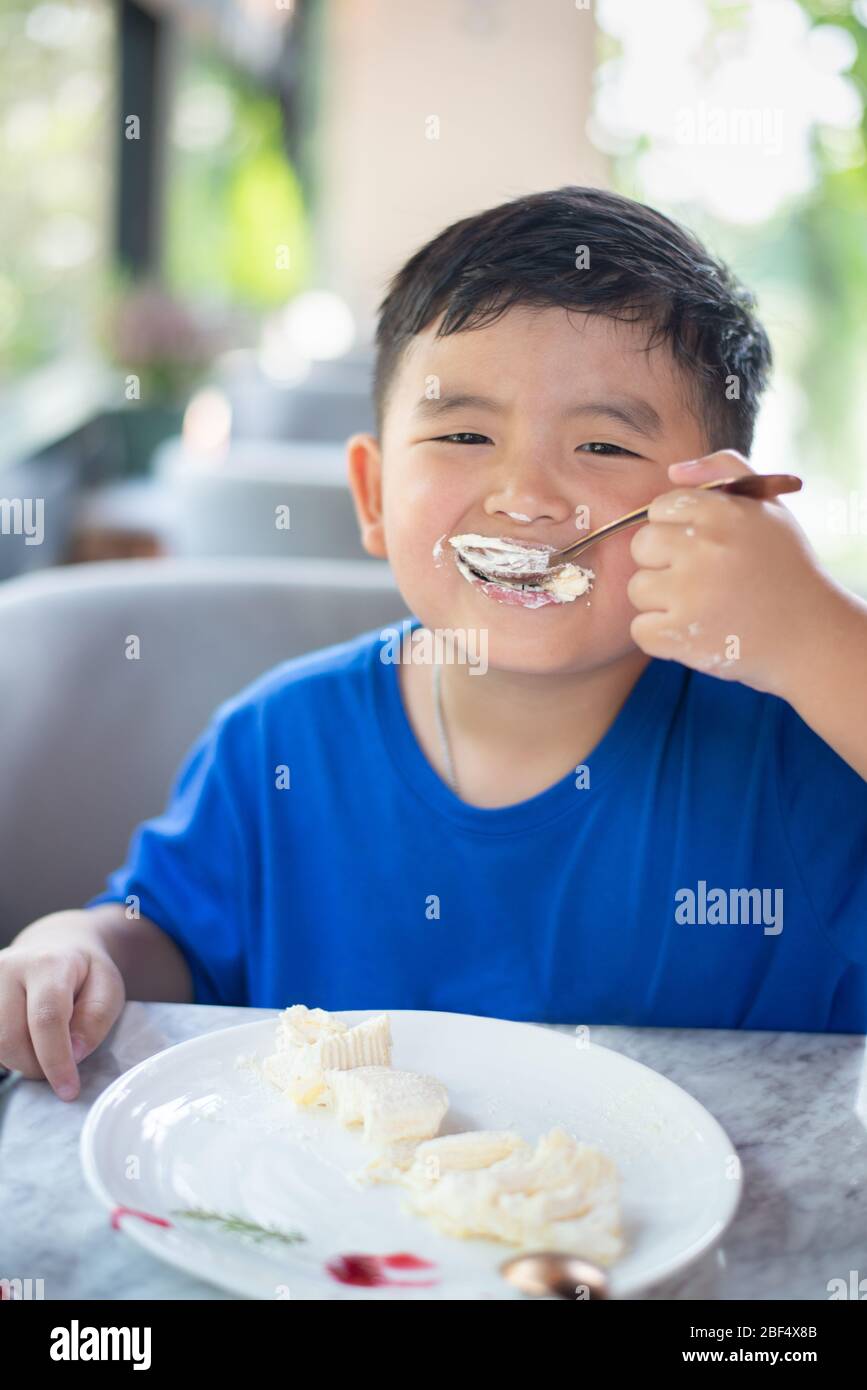 Cute little Asian boy eating cake in bakery shop or cafe Stock Photo ...