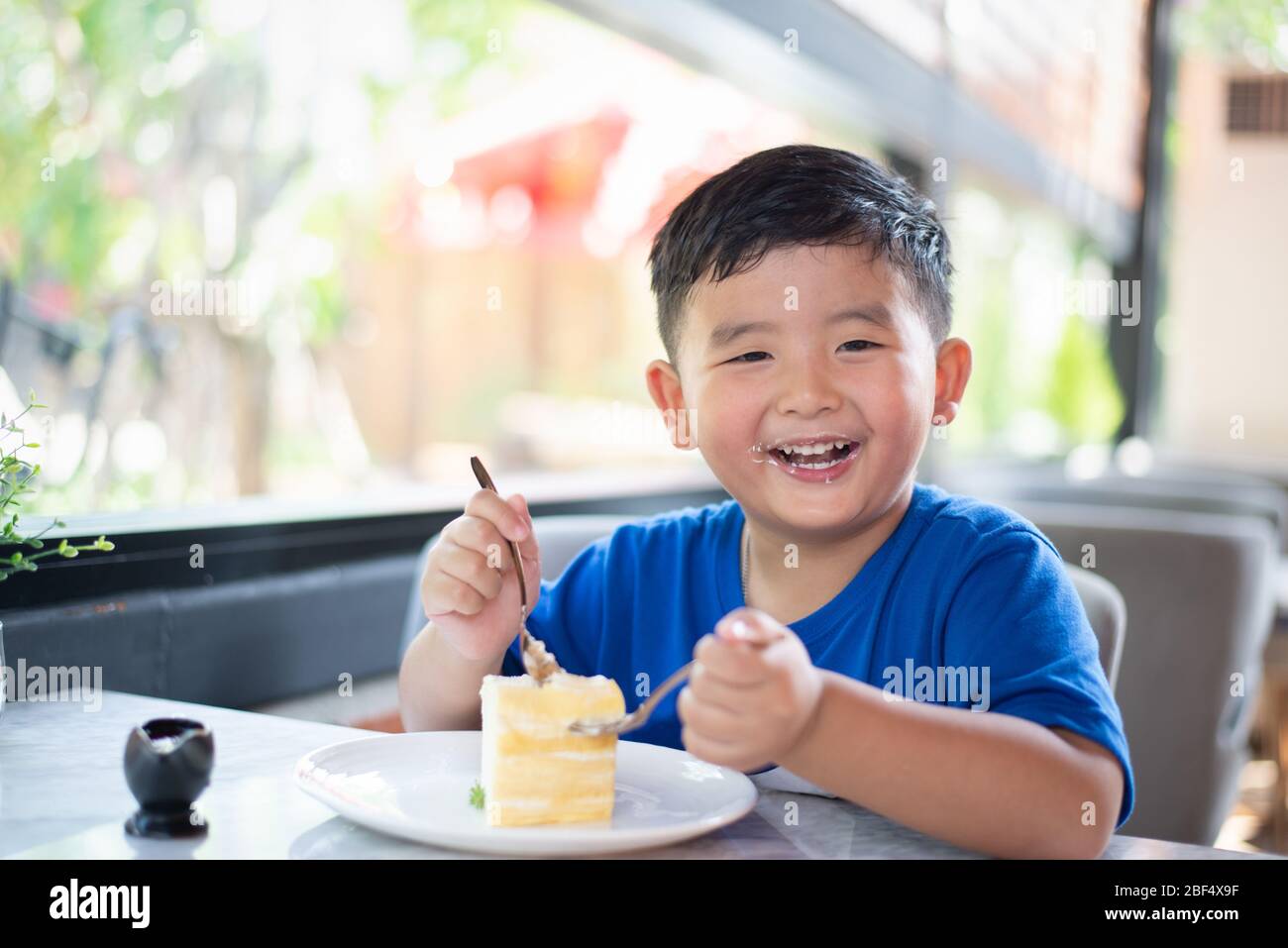 Cute little Asian boy eating cake in bakery shop or cafe Stock Photo ...