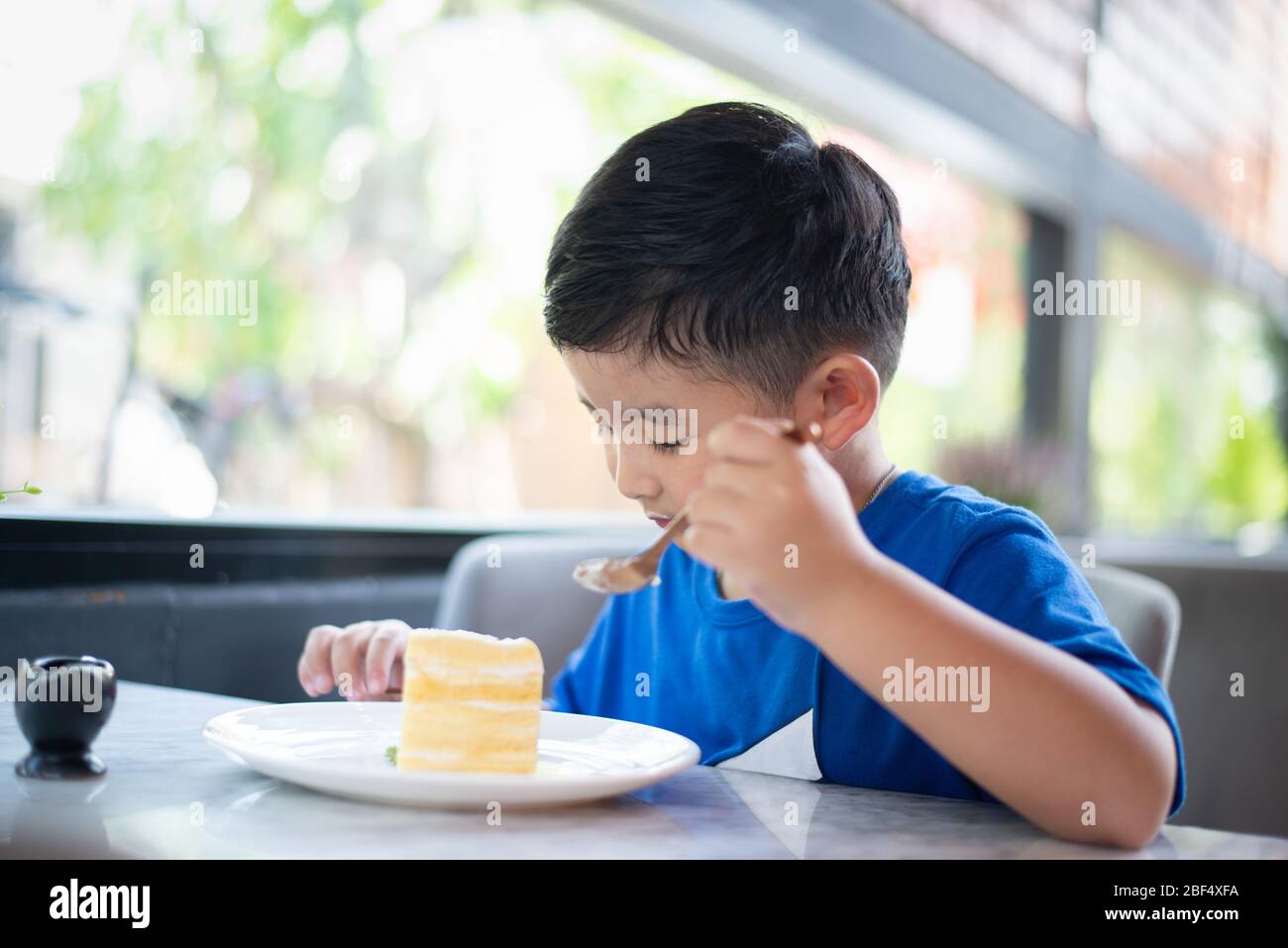 Cute little Asian boy eating cake in bakery shop or cafe Stock Photo ...