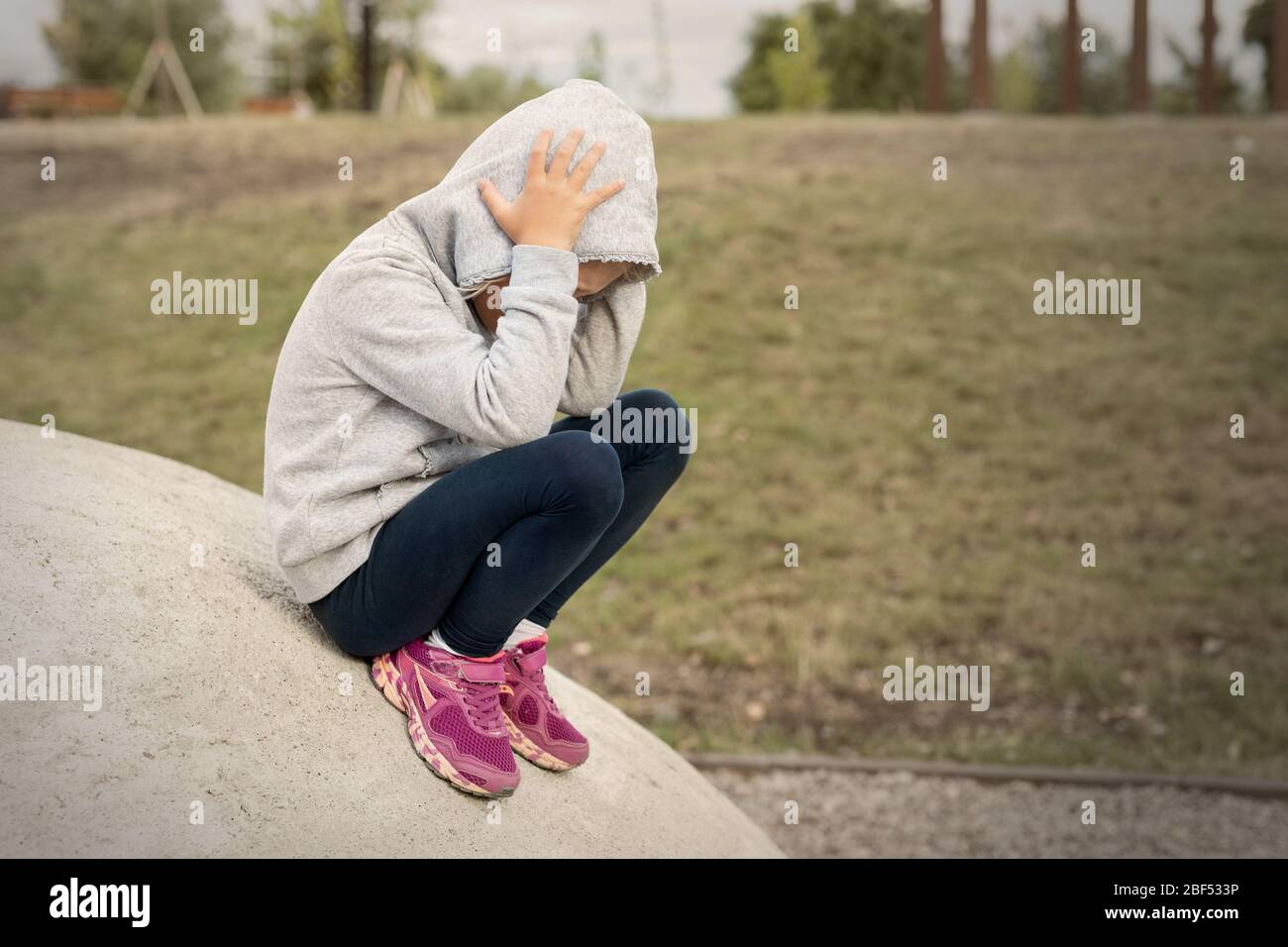 Upset sad depressed little school girl sitting alone at city street ...