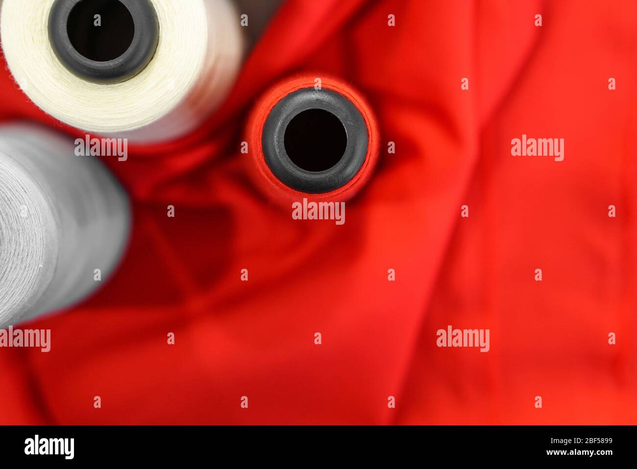 A multicolored thread spool placed on a red fine fabric. Fashion ...