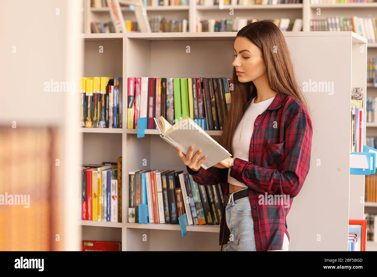 Female student reading book while preparing for exam in library Stock ...