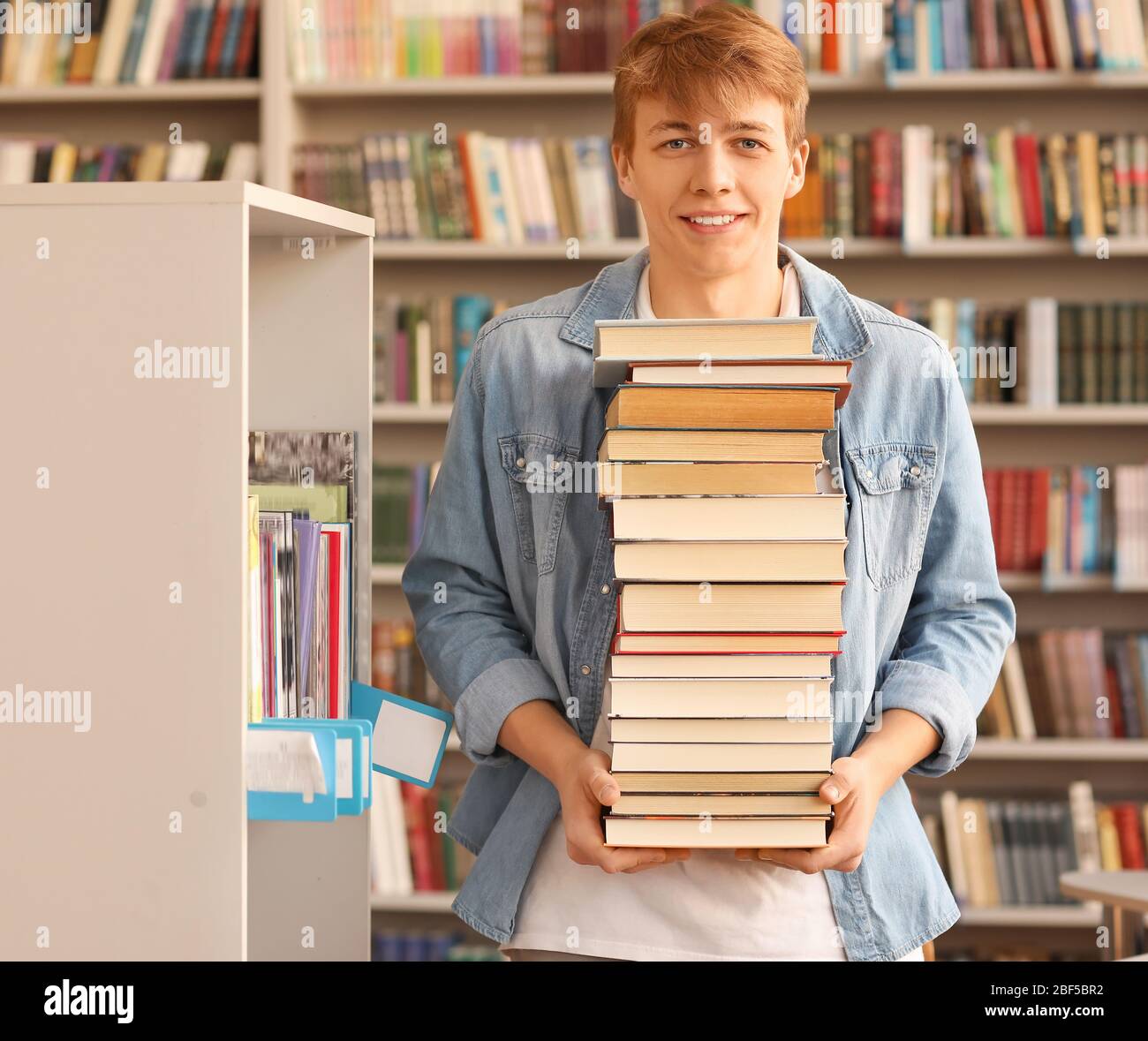 Portrait of male student with big stack of books in library Stock Photo ...