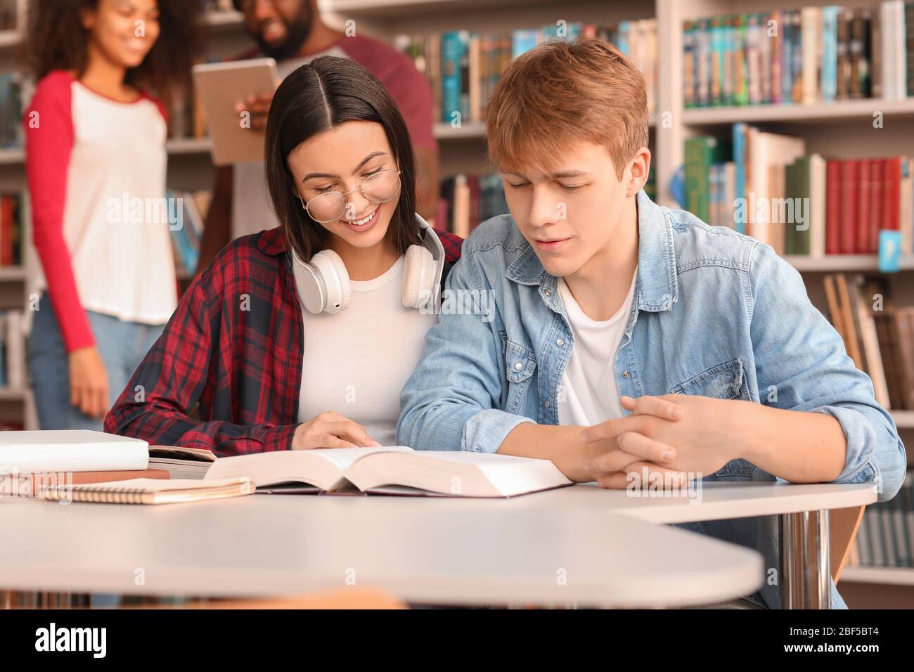 Young students reading book while preparing for exam in library Stock ...