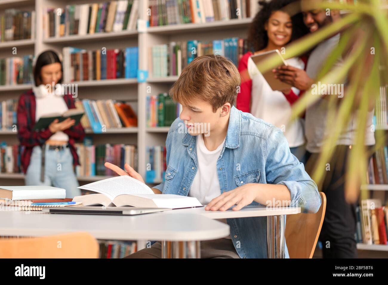 Male student reading book while preparing for exam in library Stock ...