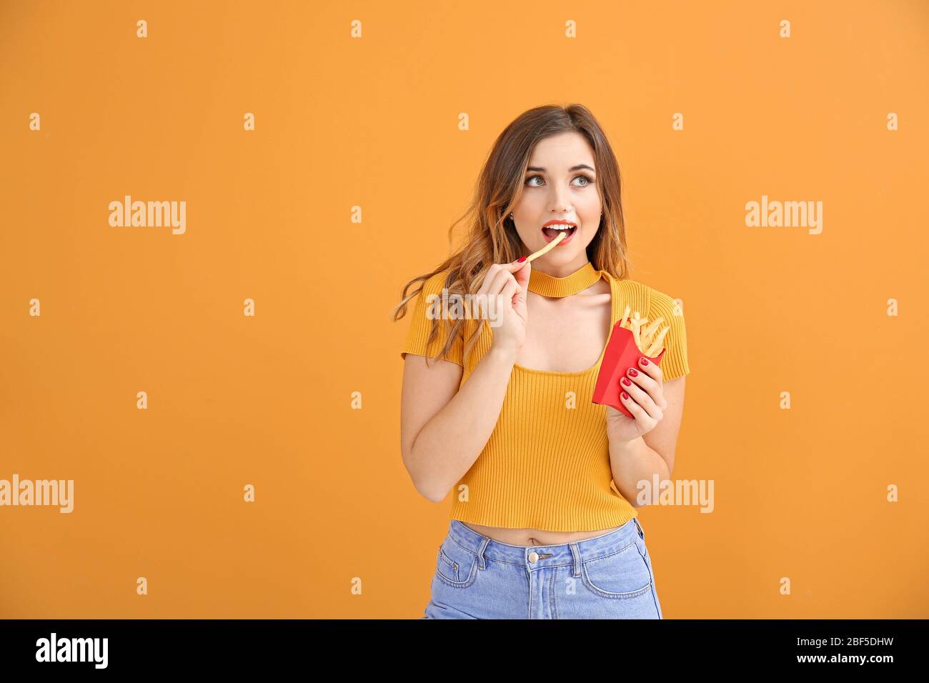 Portrait of beautiful young woman with french fries on color background ...