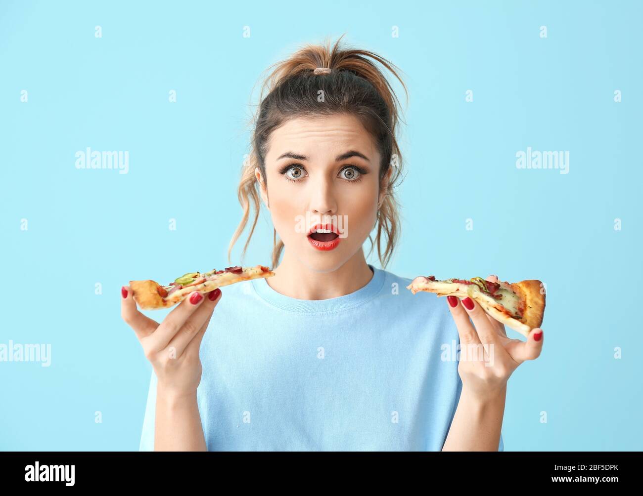 Portrait of surprised young woman eating tasty pizza on color ...