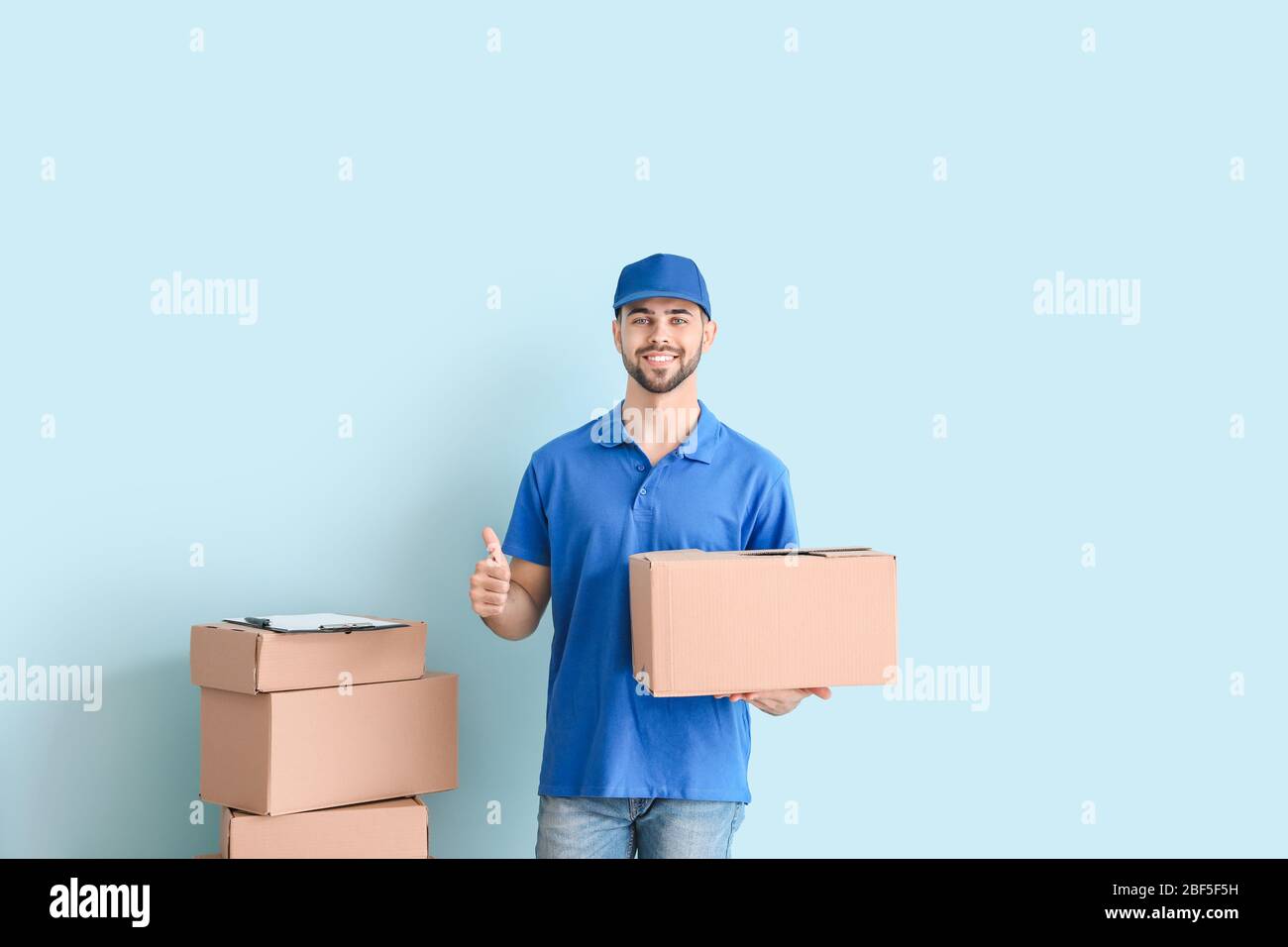 Delivery man with boxes showing thumb-up on color background Stock ...