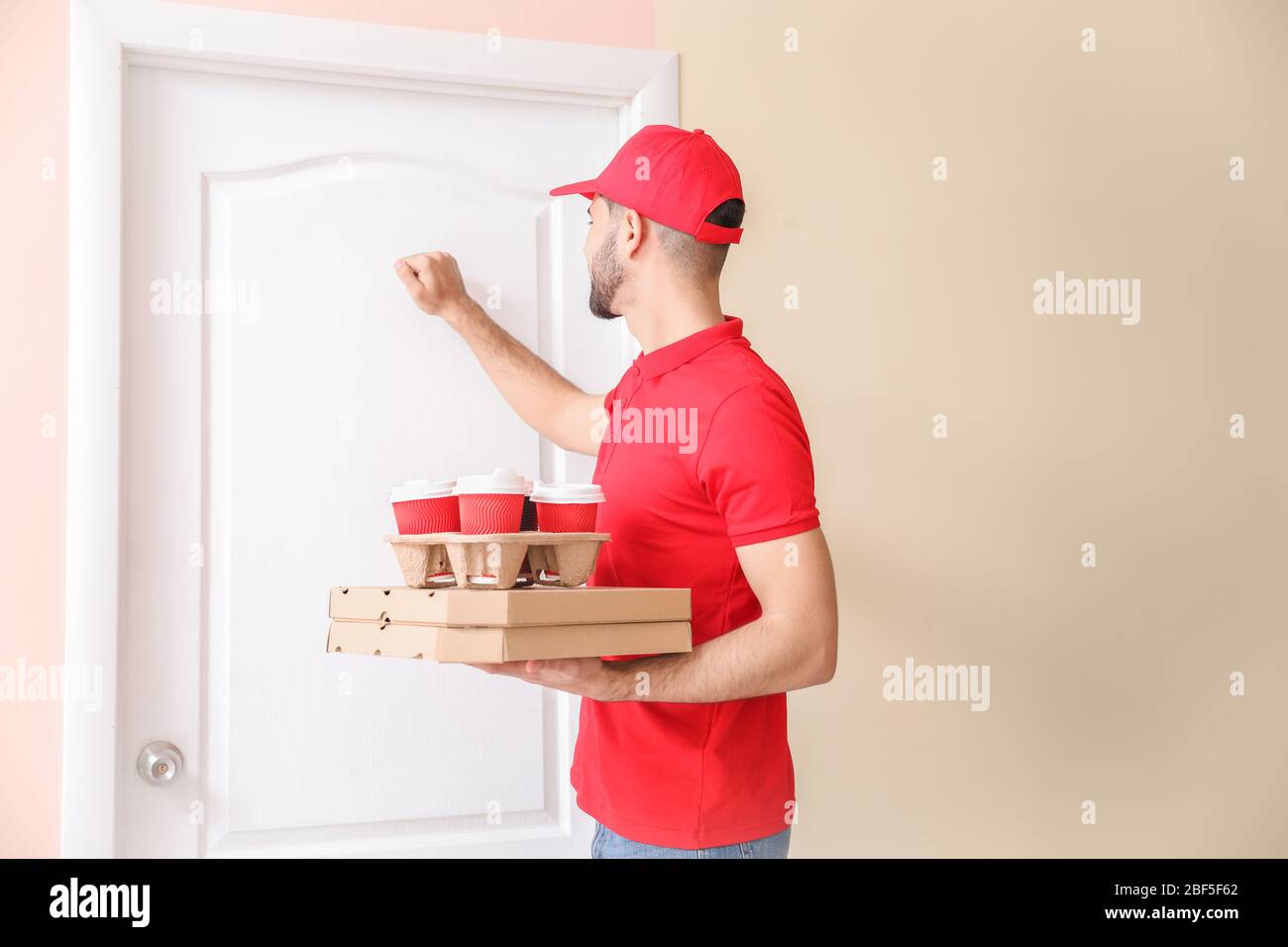 Handsome worker of food delivery service knocking at the door Stock ...