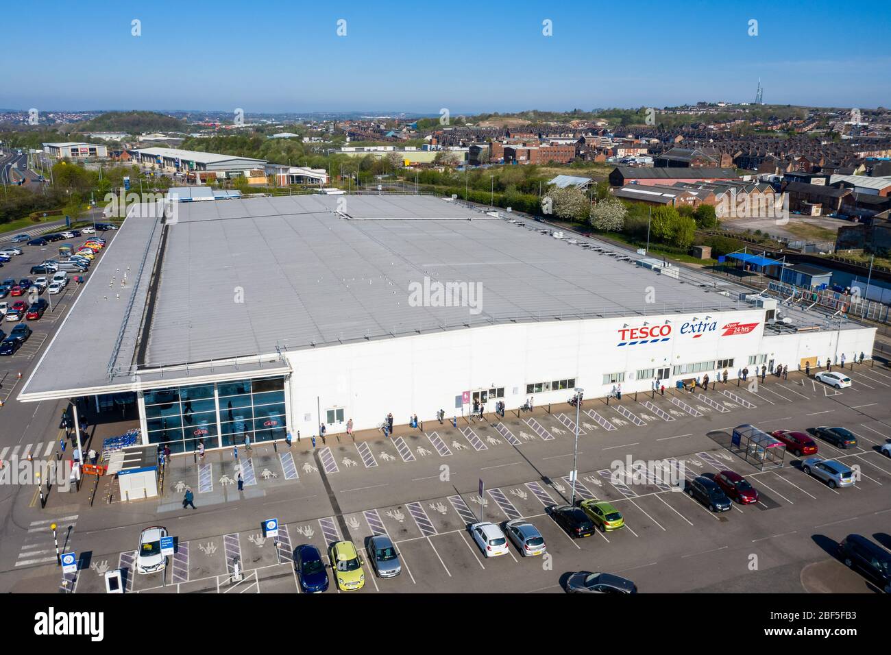 People queue 2 metres apart for a long distance outside of the Tesco ...