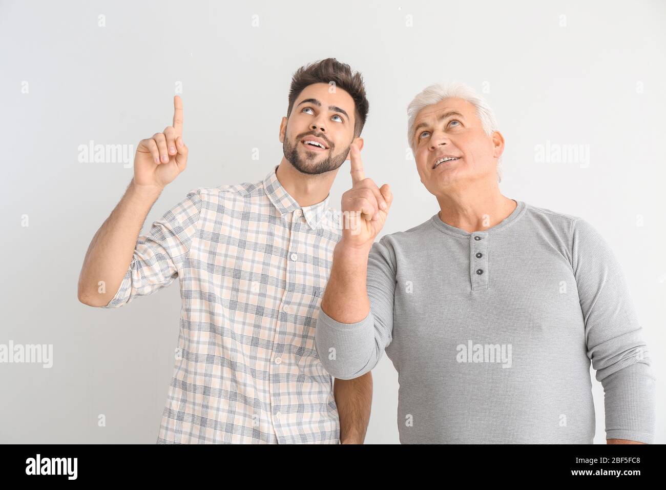 Young man and his father pointing at something on light background ...