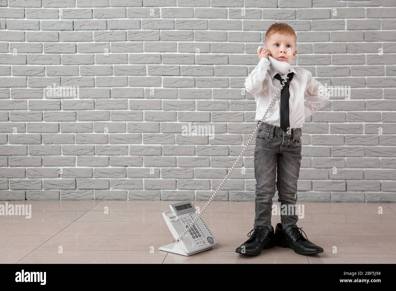 Funny little boy talking by telephone near grey wall Stock Photo - Alamy