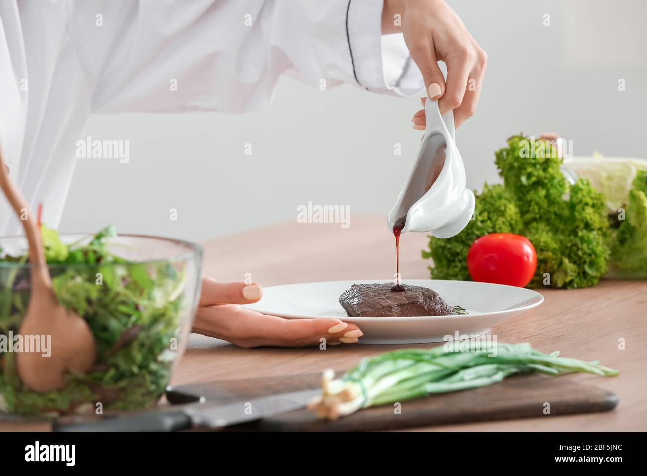 Female chef adding sauce to tasty meat in kitchen Stock Photo - Alamy