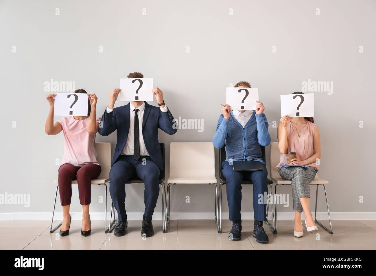 Young people holding paper sheets with question marks while sitting on ...