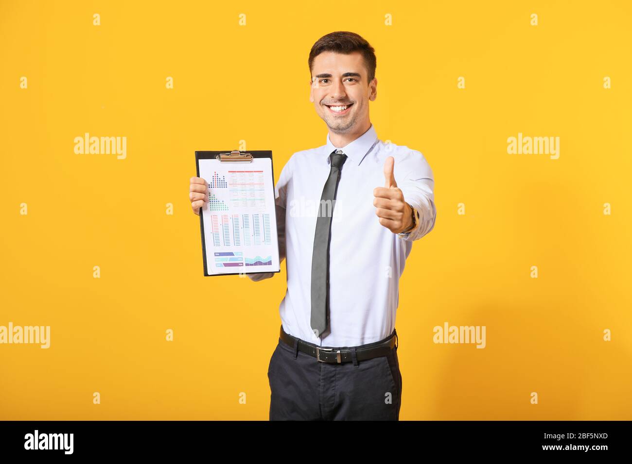 Male bank manager with document showing thumb-up gesture on color ...