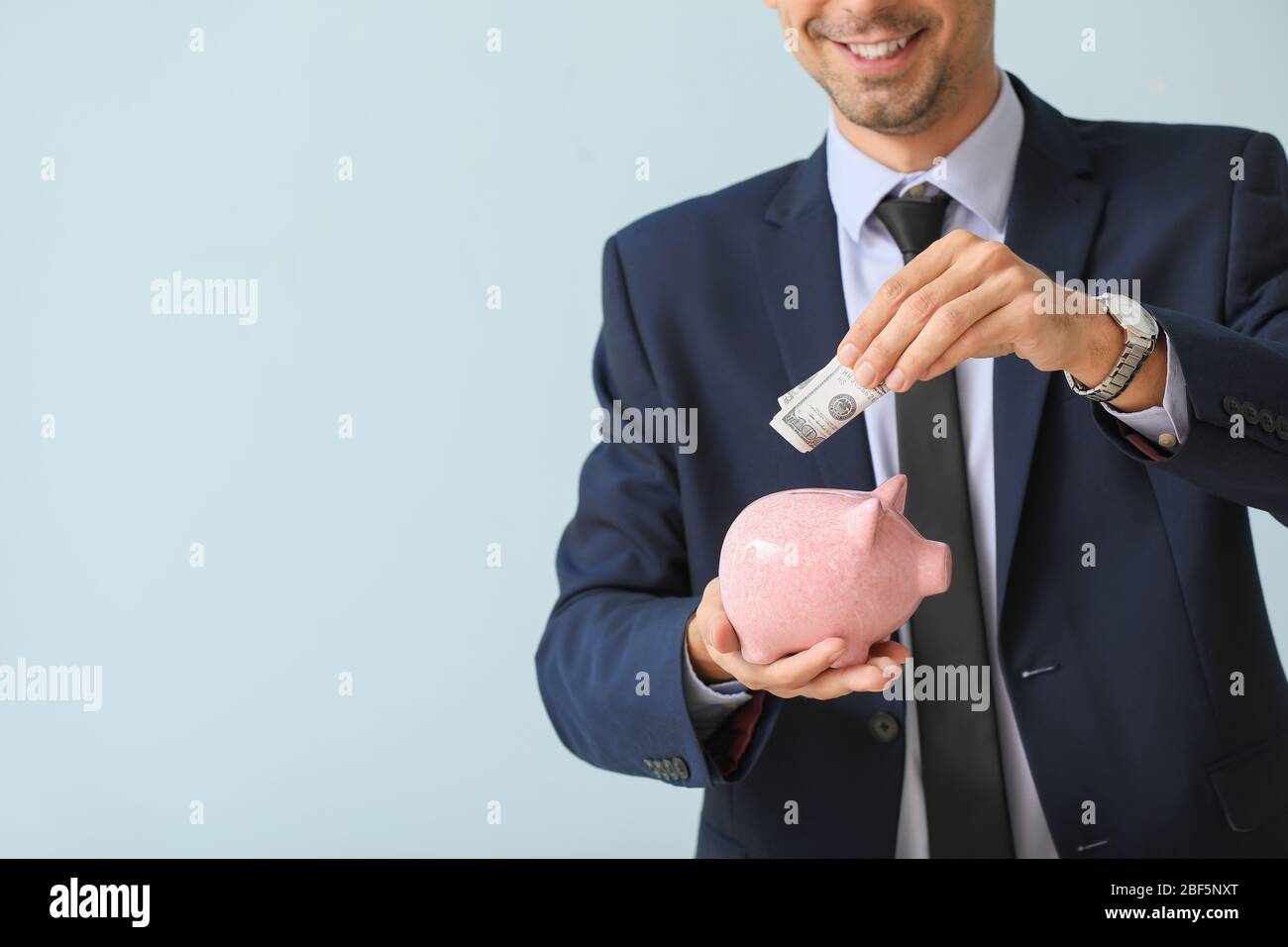 Male bank manager putting money in piggy bank on light background Stock ...