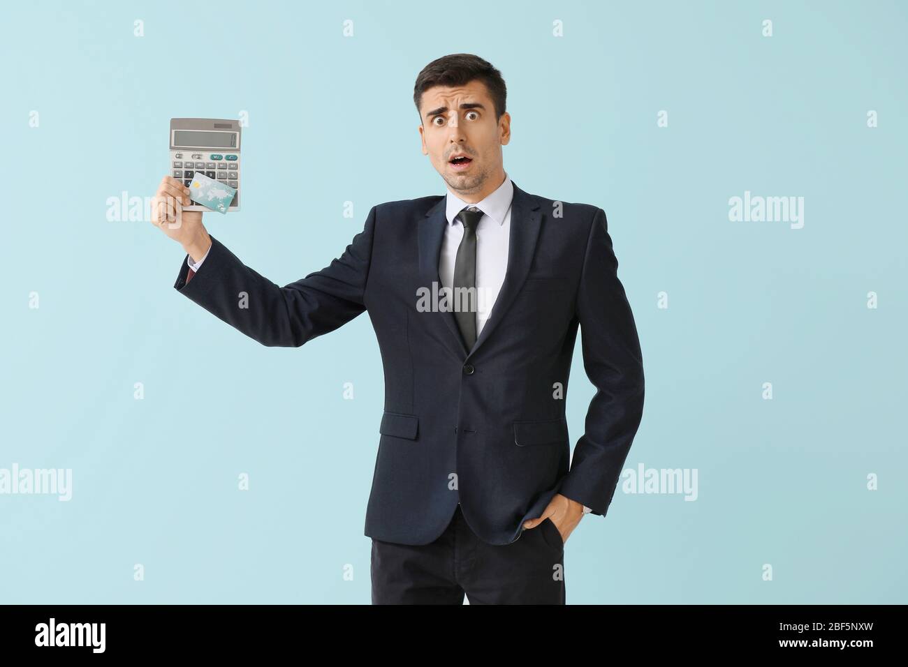 Afraid male bank manager with credit card and calculator on light ...