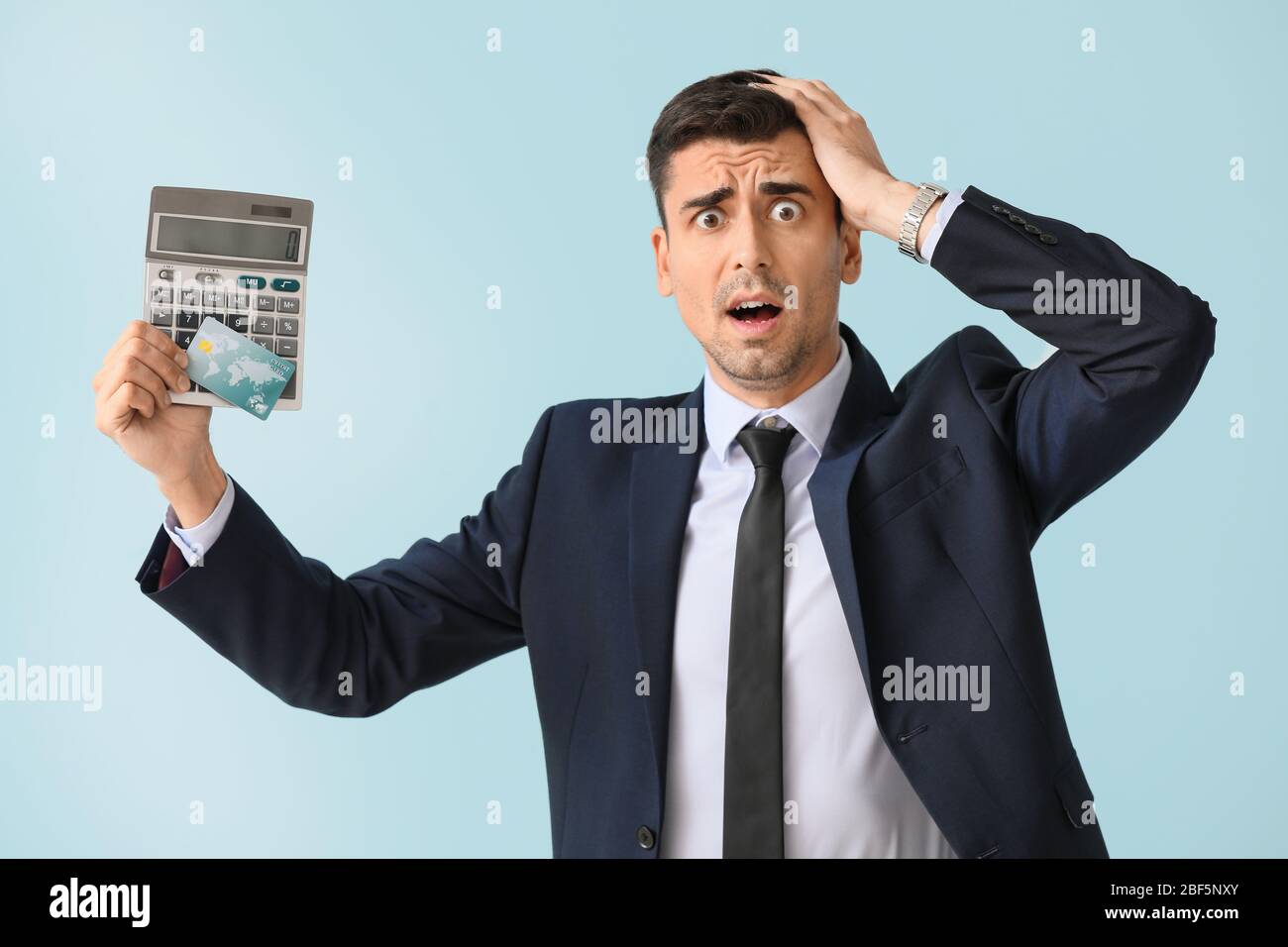 Afraid male bank manager with credit card and calculator on light ...