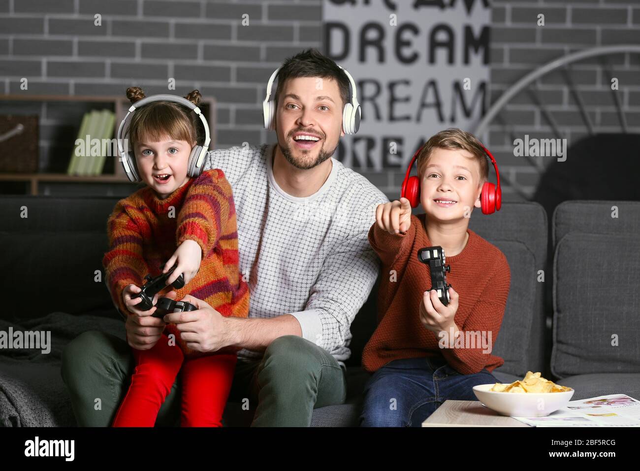Father and his little children playing video games at home in evening ...