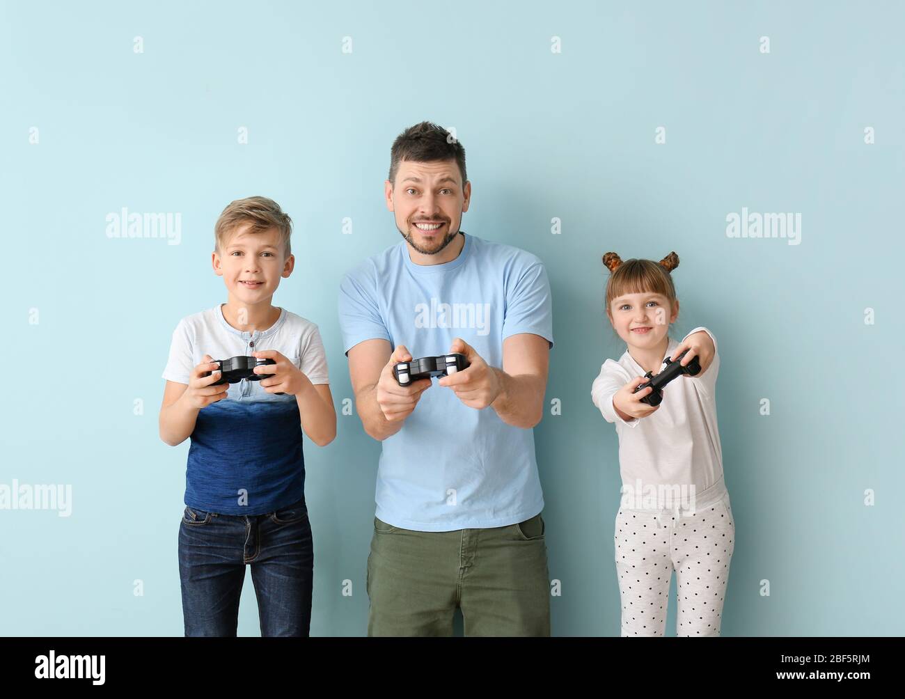 Father and his little children playing video games on color background ...