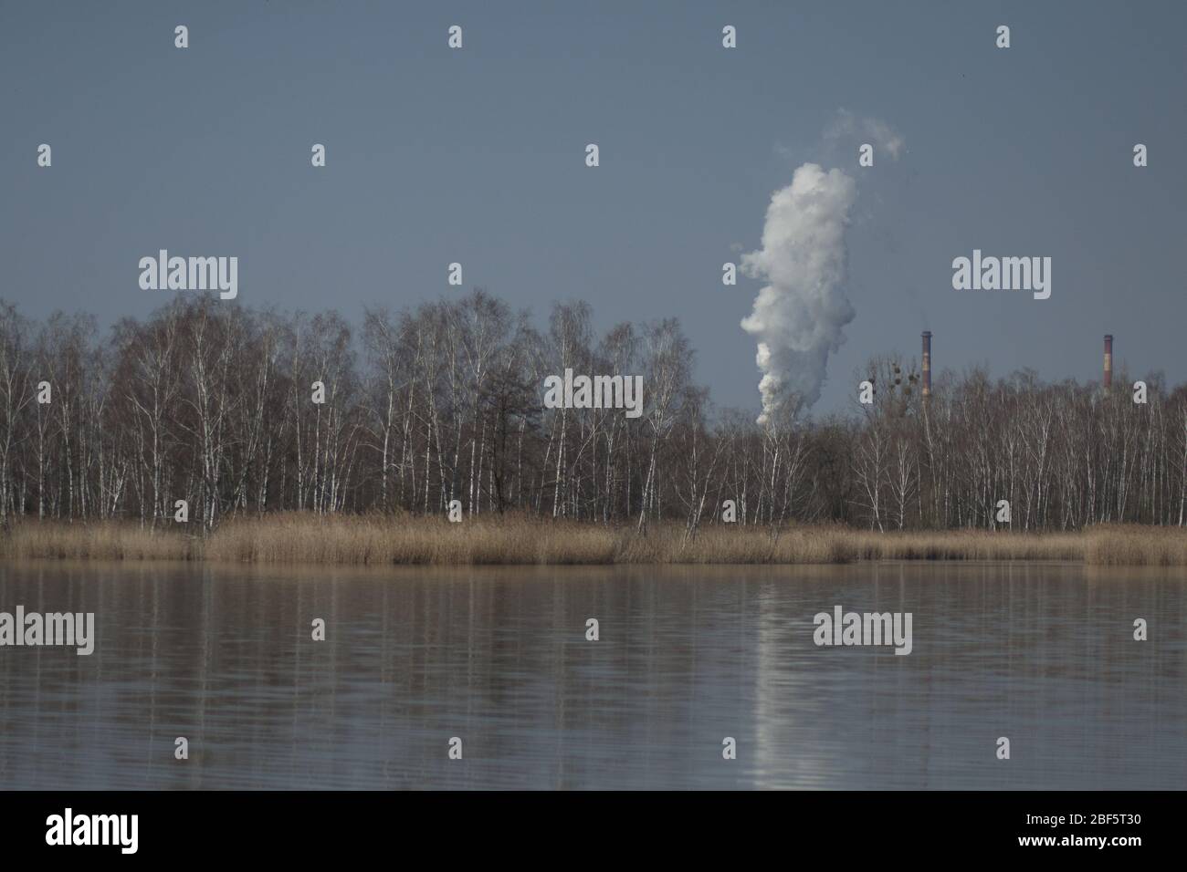 Steam clouds floating from the factory against the blue sky and near ...