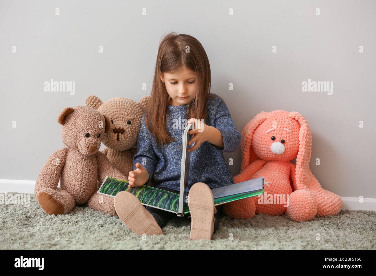 Cute little girl with toys reading book at home Stock Photo - Alamy