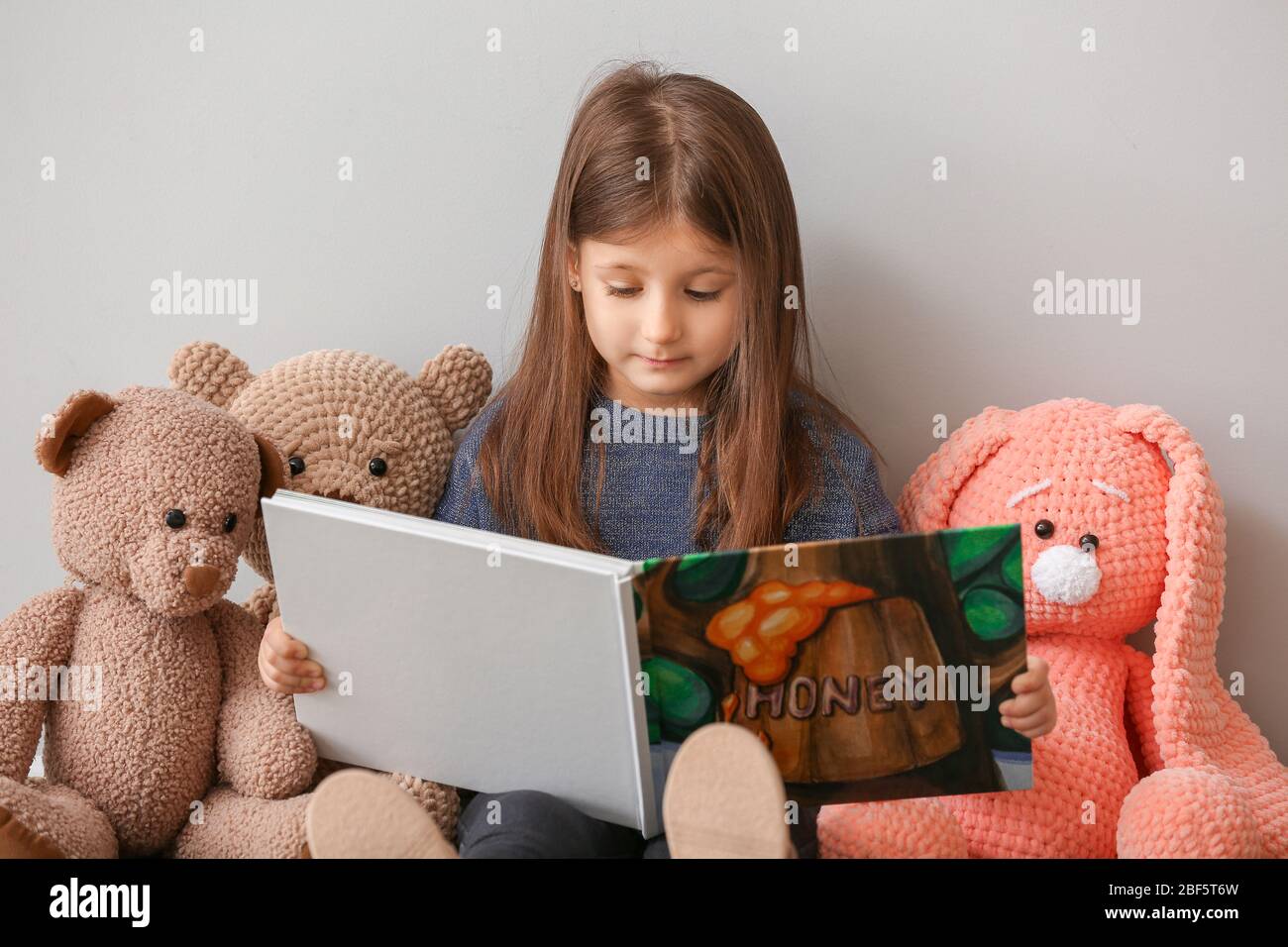 Cute little girl with toys reading book at home Stock Photo - Alamy