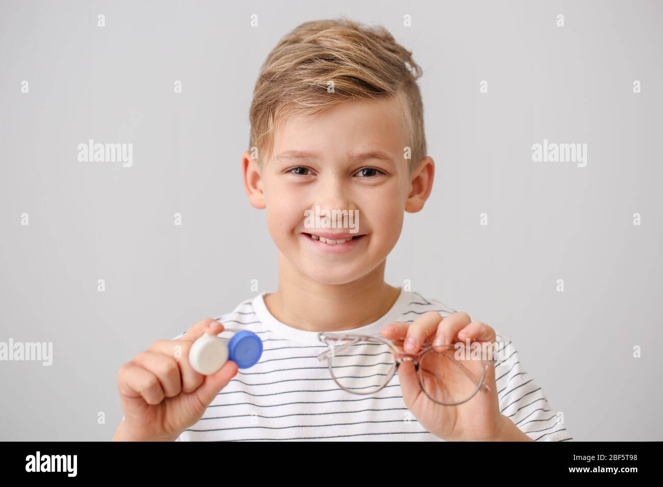 Little boy with contact lens case and eyeglasses on grey background ...