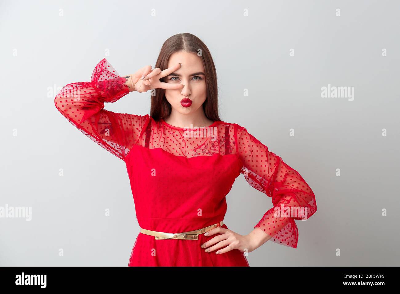 Emotional young woman showing victory gesture on light background Stock ...