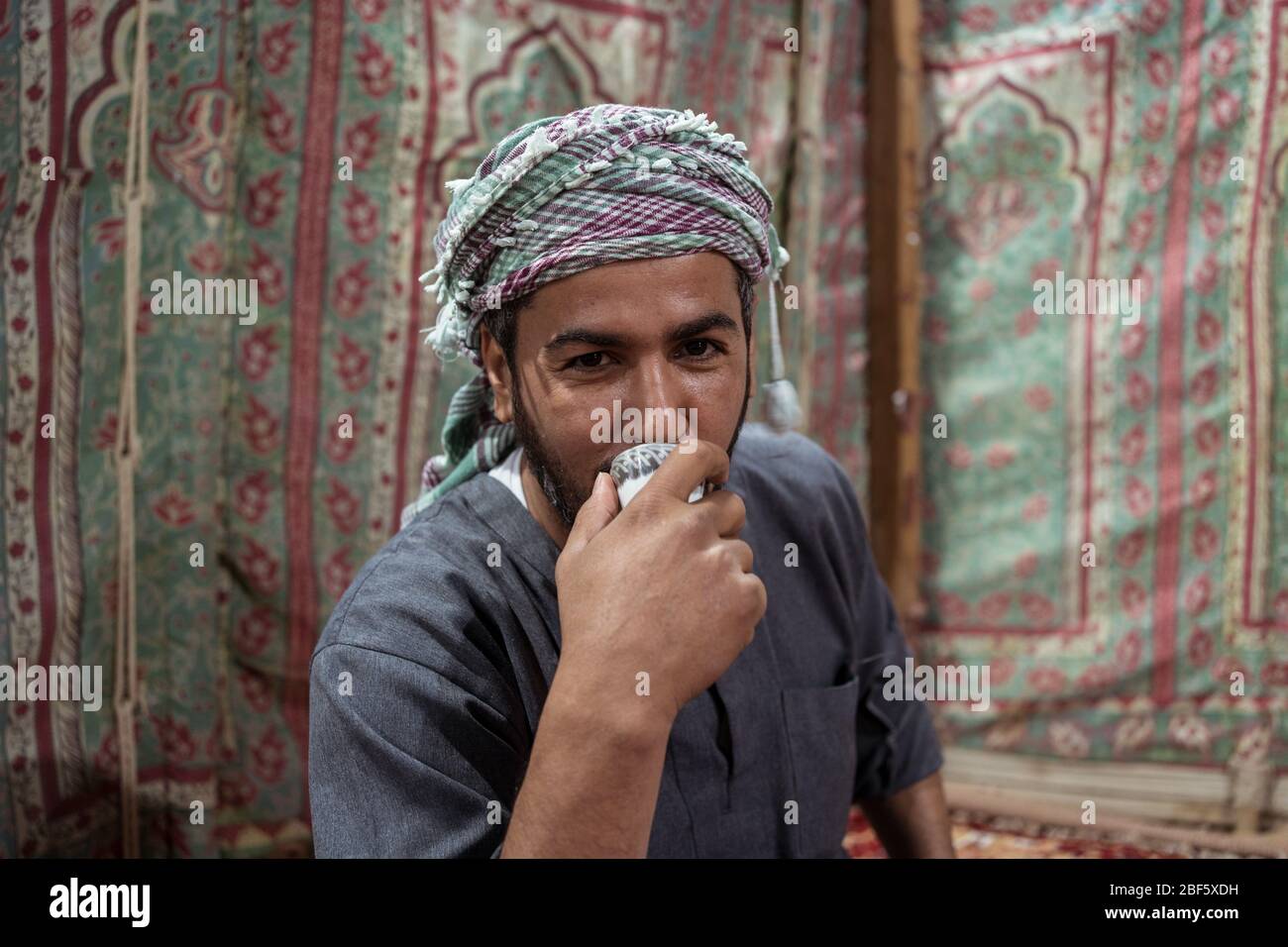 Bedouin man wearing traditional clothes drinks tea on a carpet in the ...