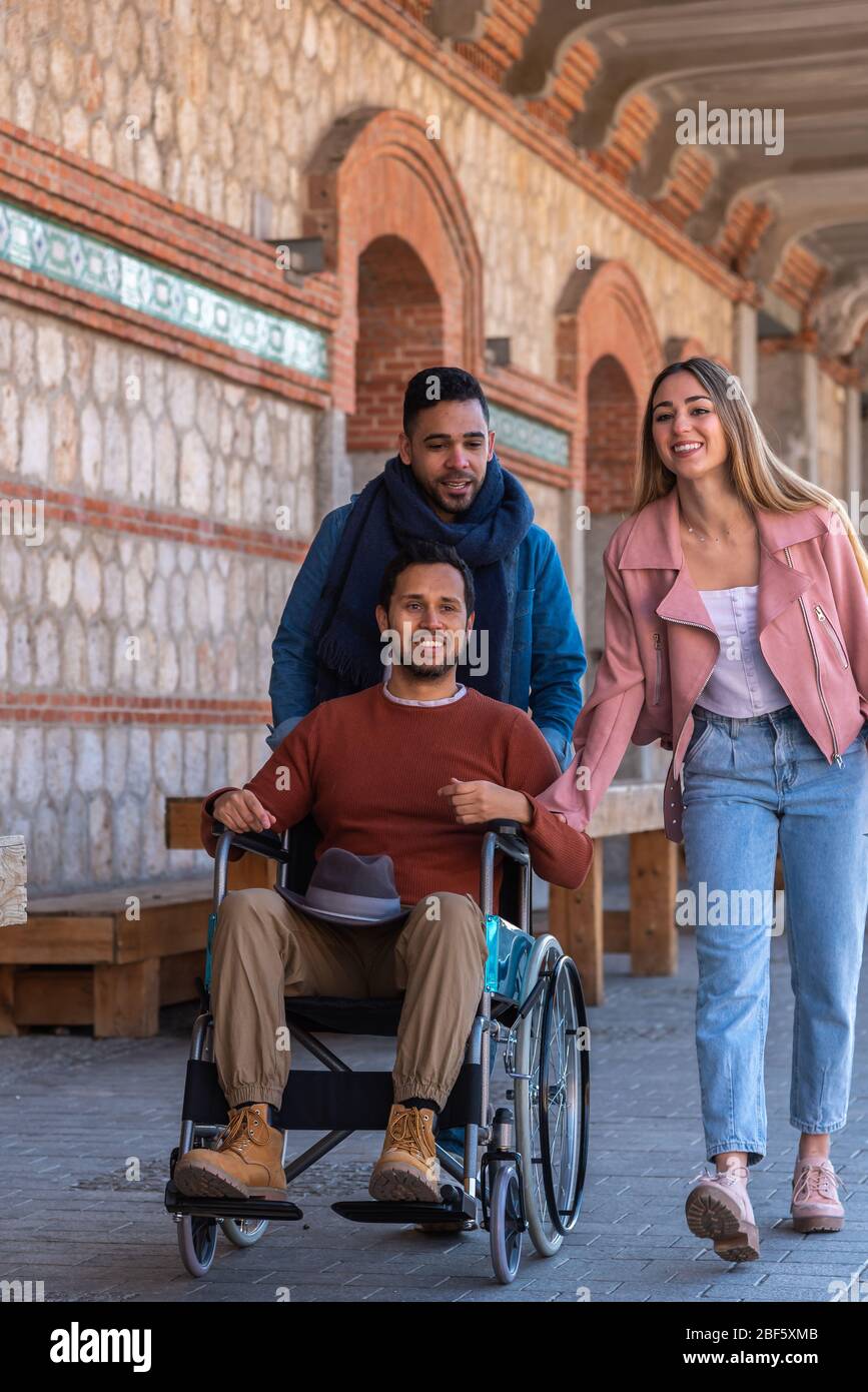 A young paralyzed Latino boy in a wheelchair accompanied by a young ...