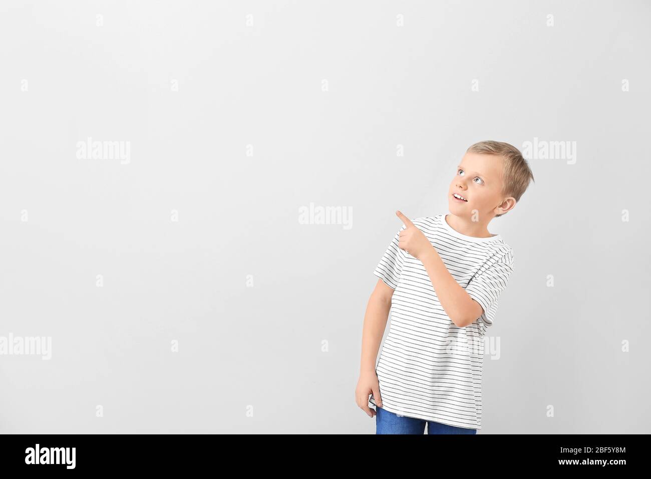 Cute little boy pointing at something on light background Stock Photo ...