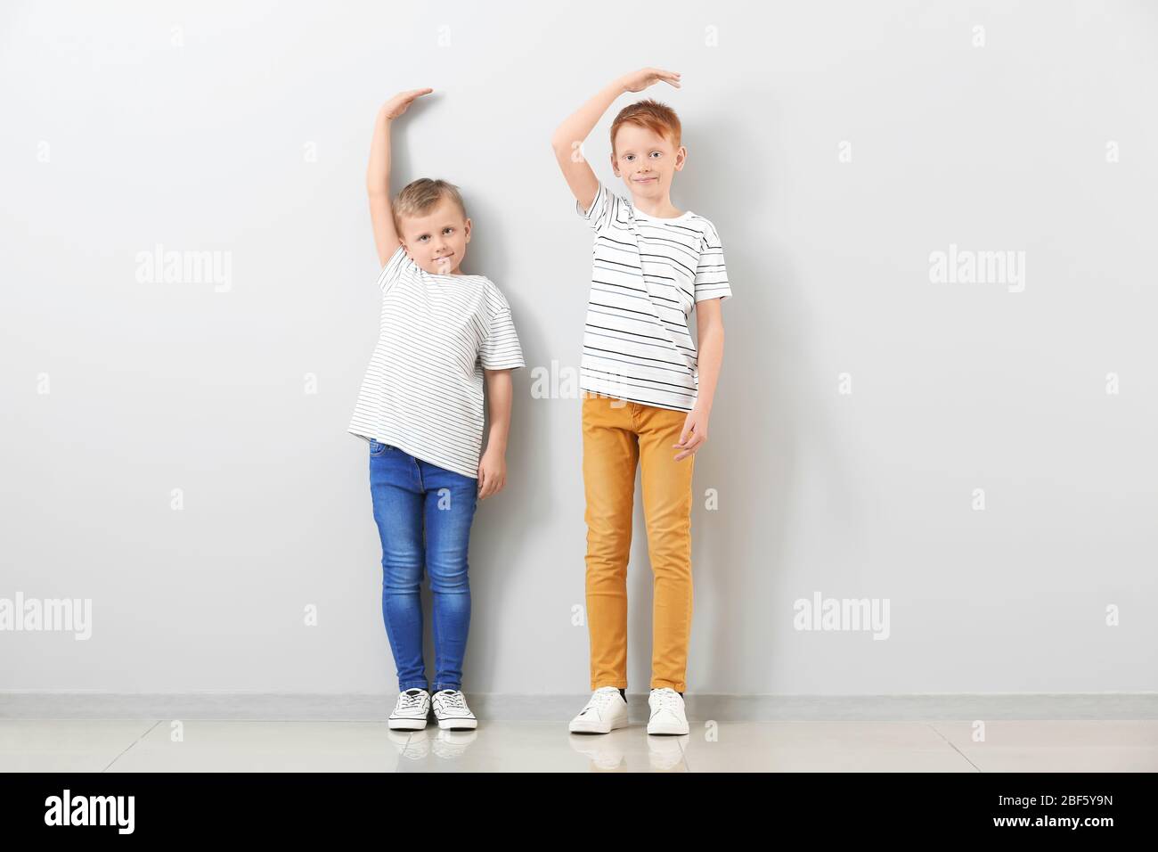 Cute little boys measuring height near light wall Stock Photo - Alamy