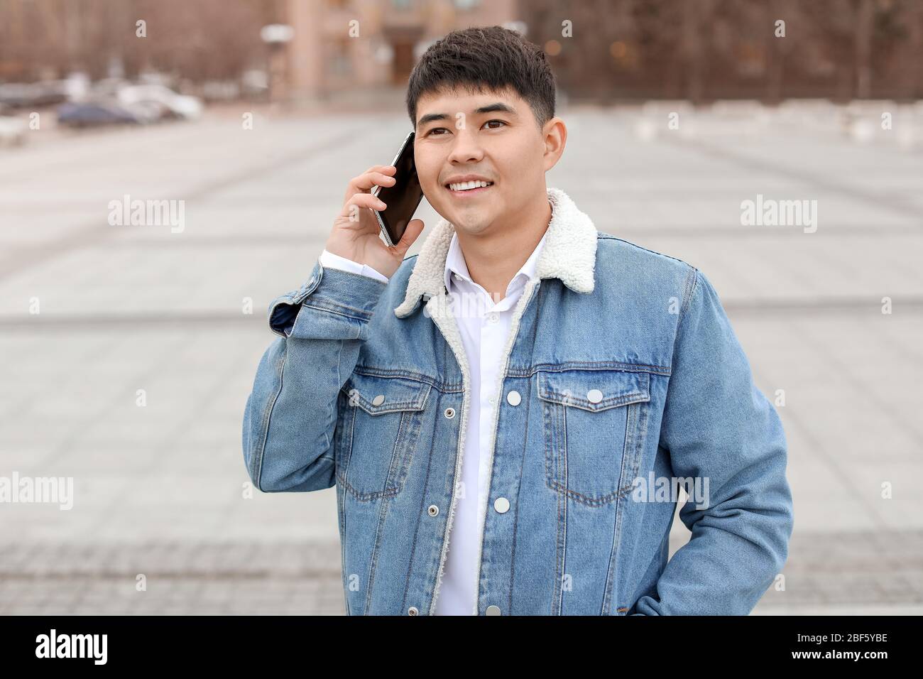 Young Asian man talking by mobile phone outdoors Stock Photo - Alamy