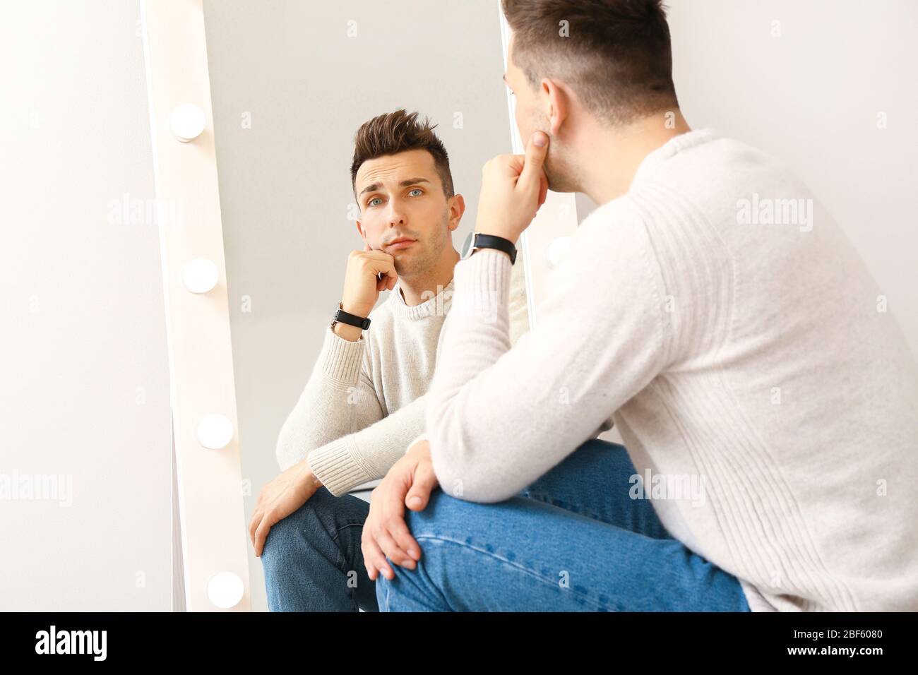 Thoughtful young man looking at his reflection in mirror Stock Photo ...