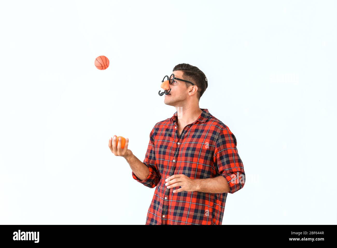Man in funny disguise juggling with balls on light background. April ...