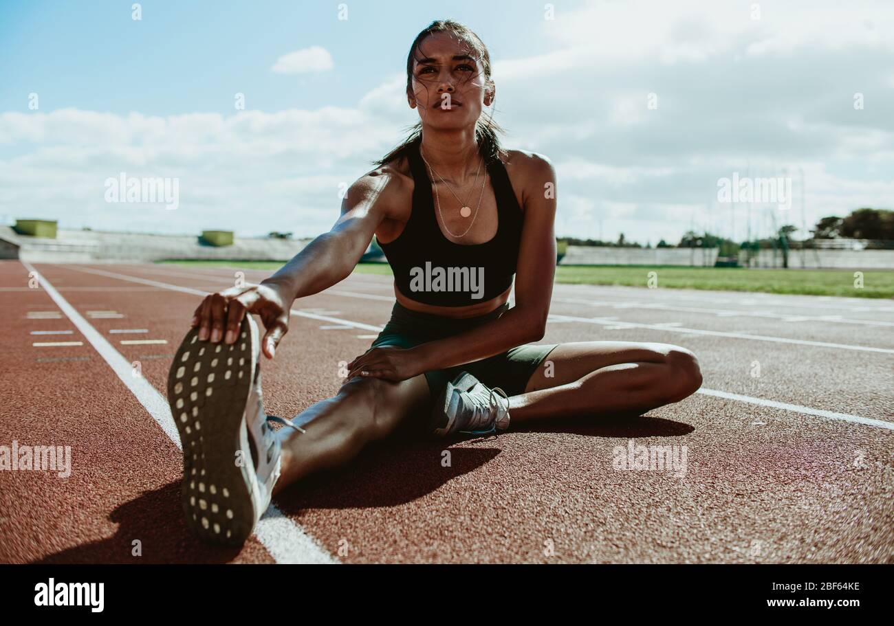 Female runner doing stretching exercises sitting on running track ...
