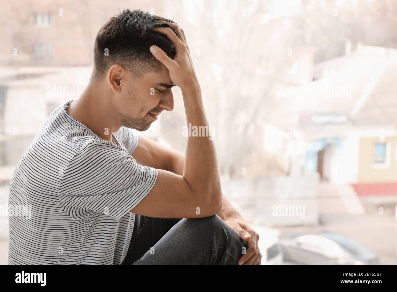 Depressed young man near window Stock Photo - Alamy