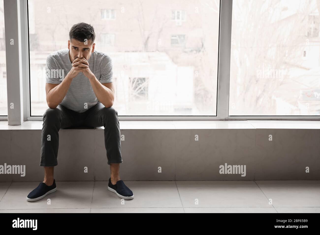 Depressed young man near window Stock Photo - Alamy