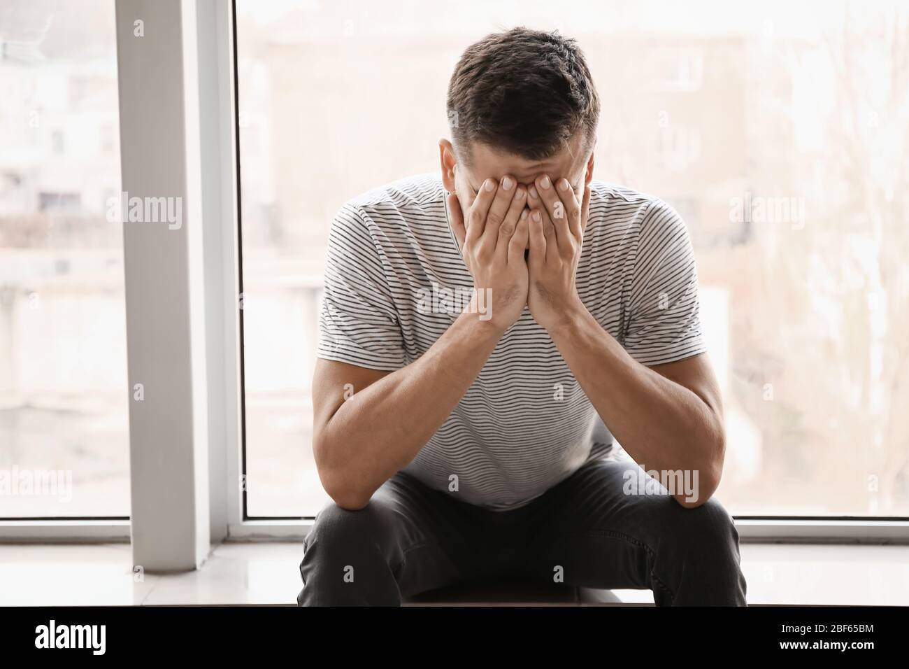 Depressed young man near window Stock Photo - Alamy