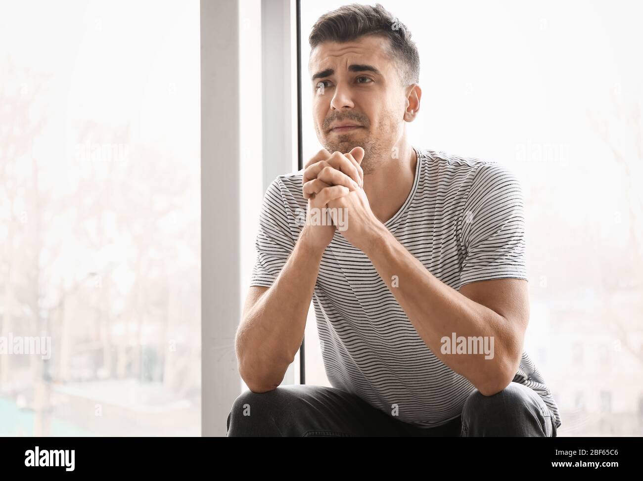 Depressed young man near window Stock Photo - Alamy