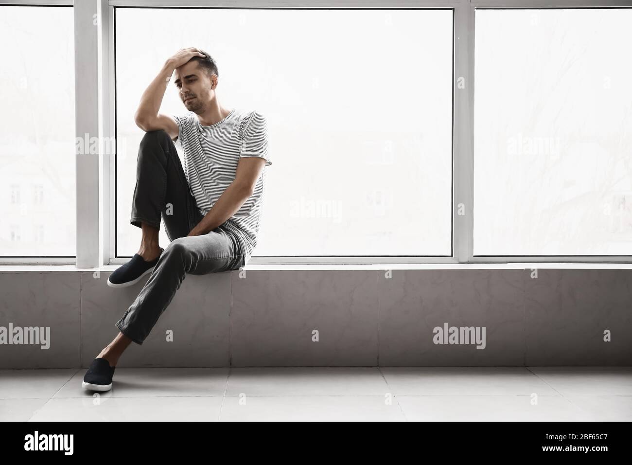 Depressed young man near window Stock Photo - Alamy