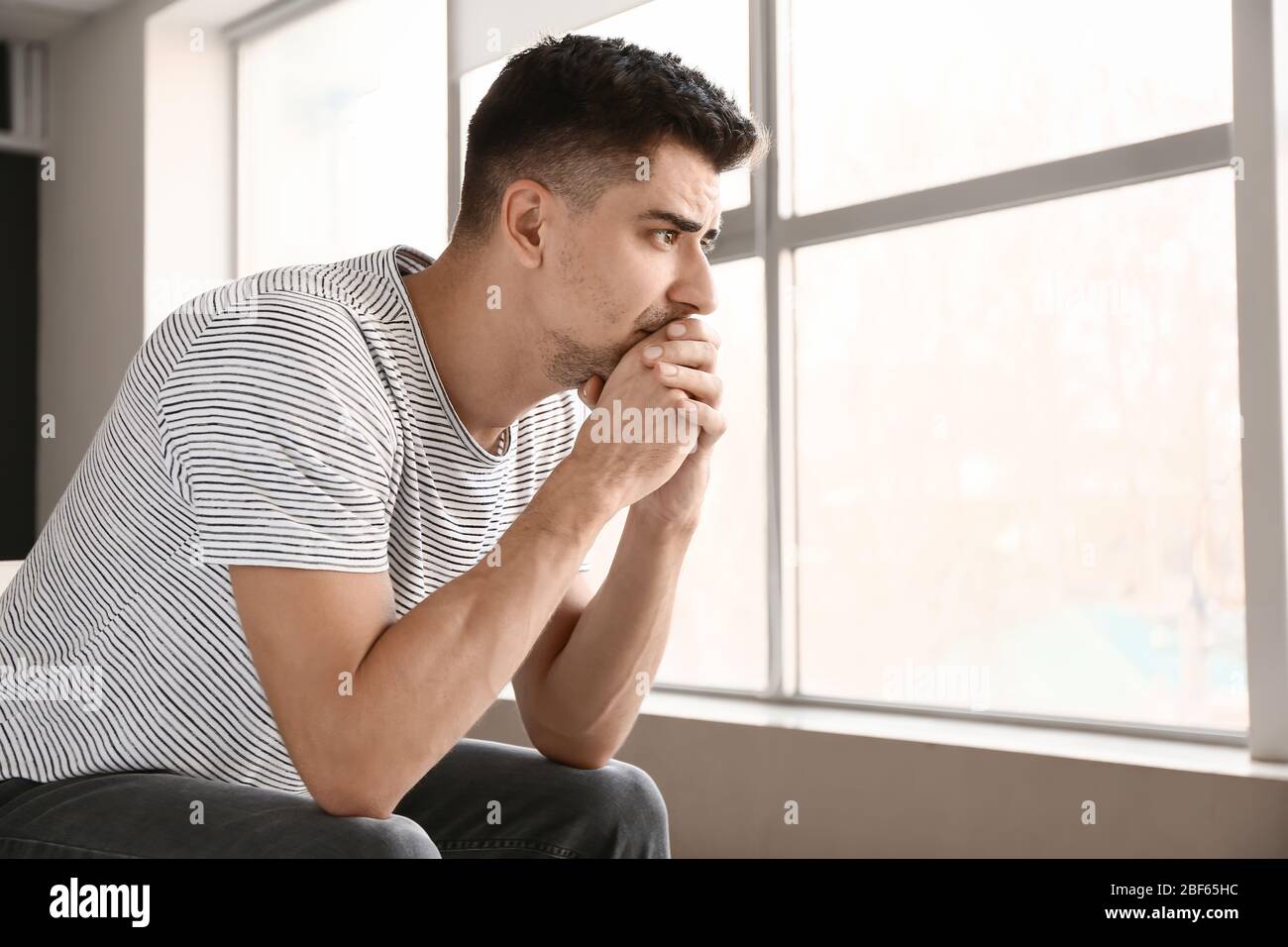 Depressed young man near window Stock Photo - Alamy