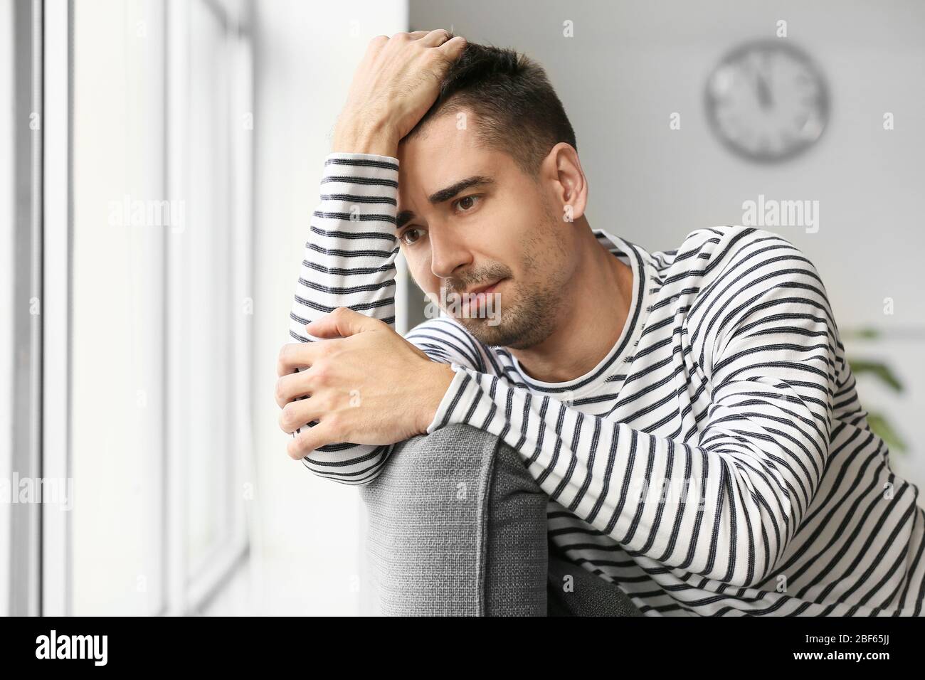 Depressed young man near window at home Stock Photo - Alamy