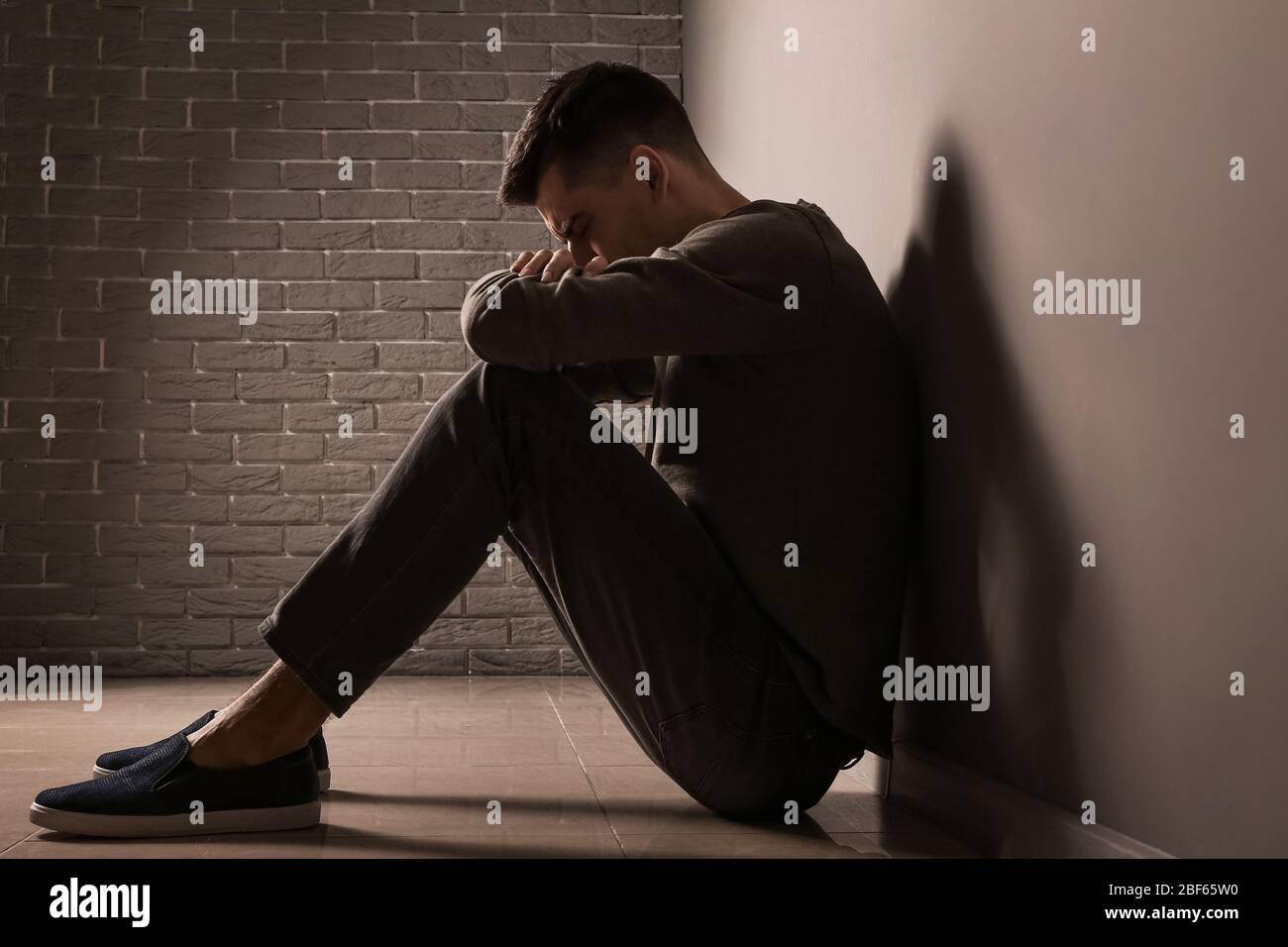 Depressed young man near grey wall Stock Photo - Alamy